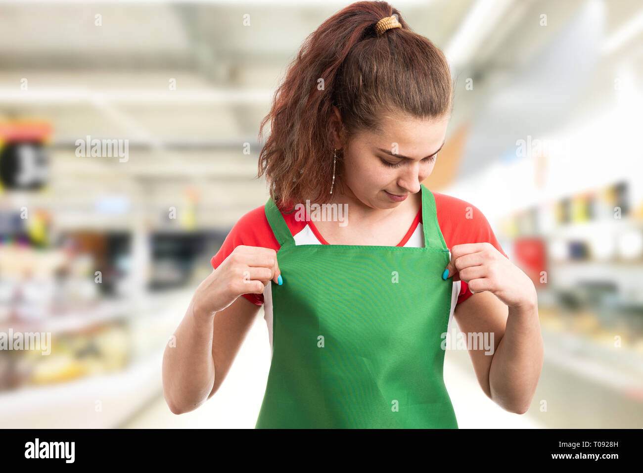 Female hypermarket or supermarket employee fixing green apron as ...