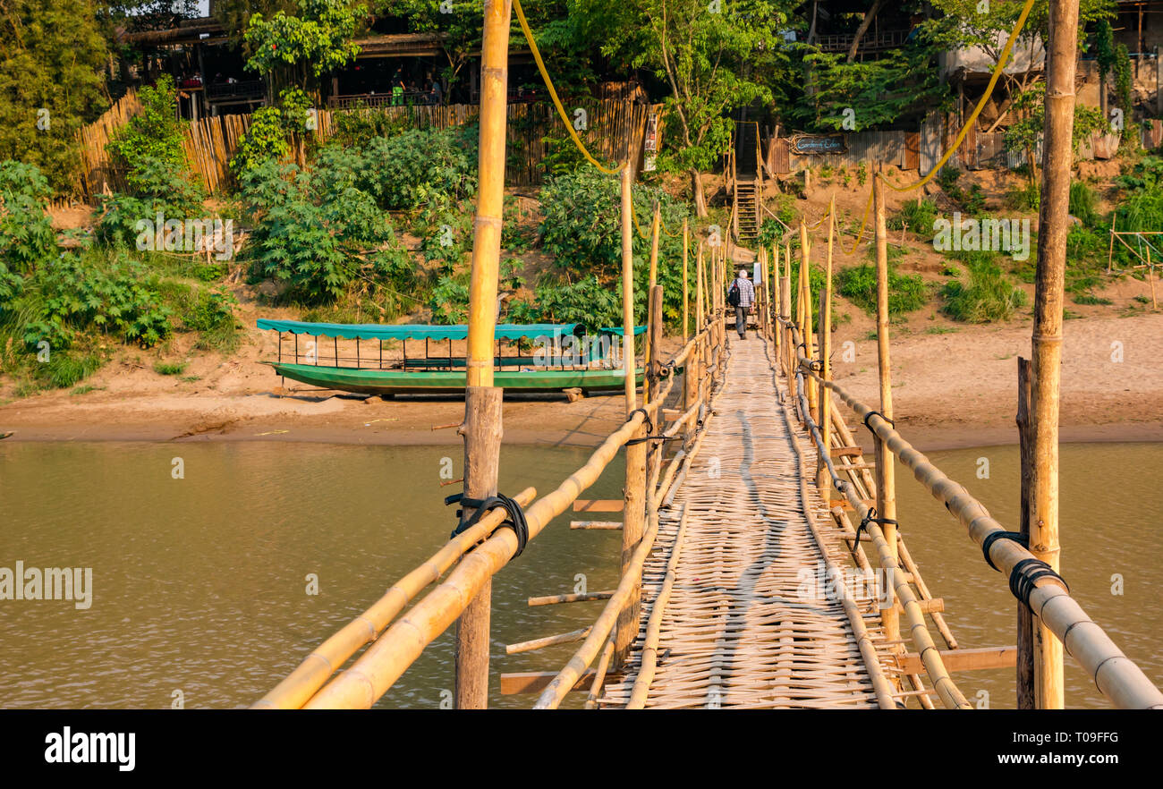 Senior male tourist walking across rickety bamboo cane bridge over Nam ...