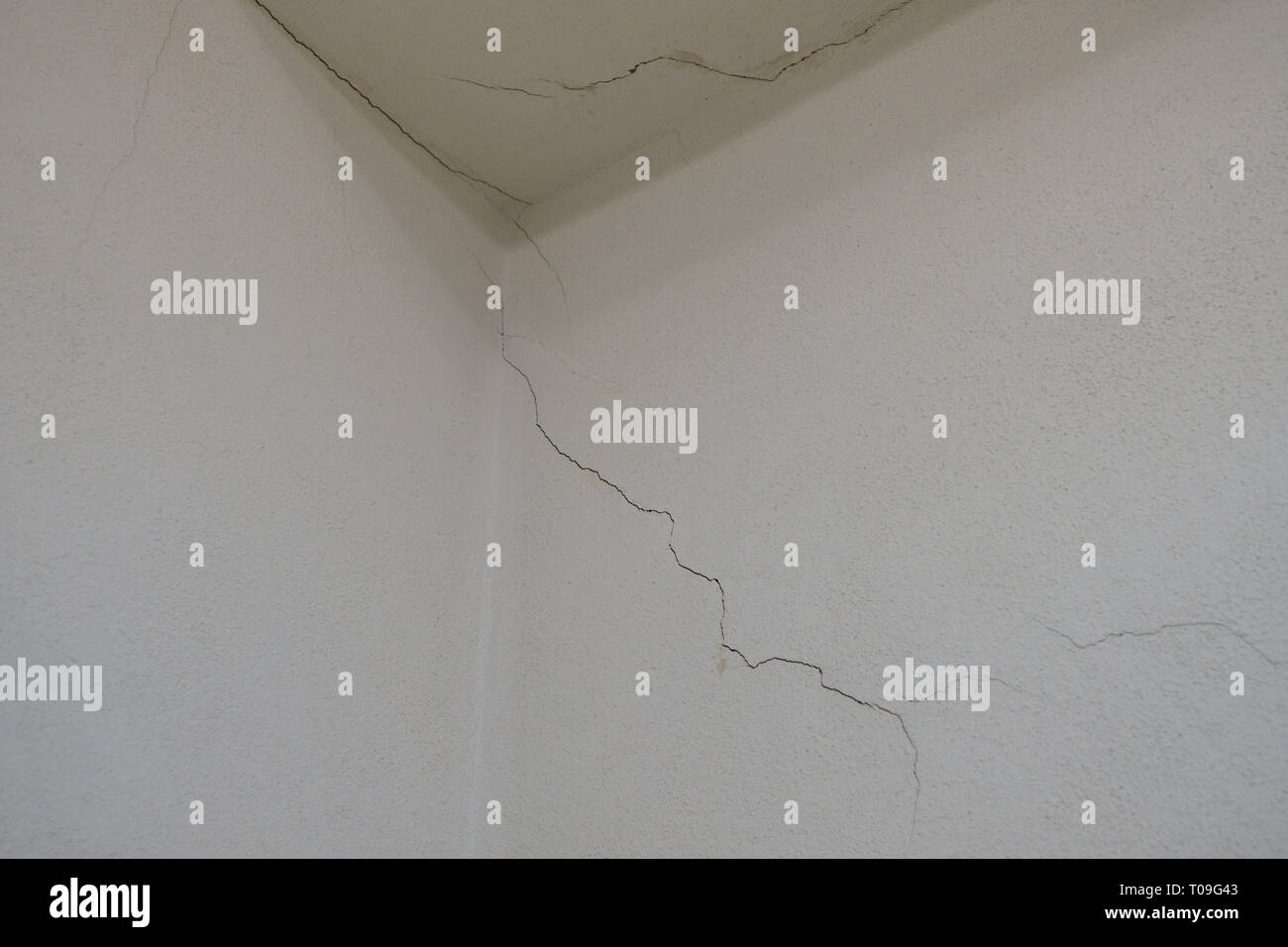 Uper corner of a white room with cracks on the wall, showing signs of a ...