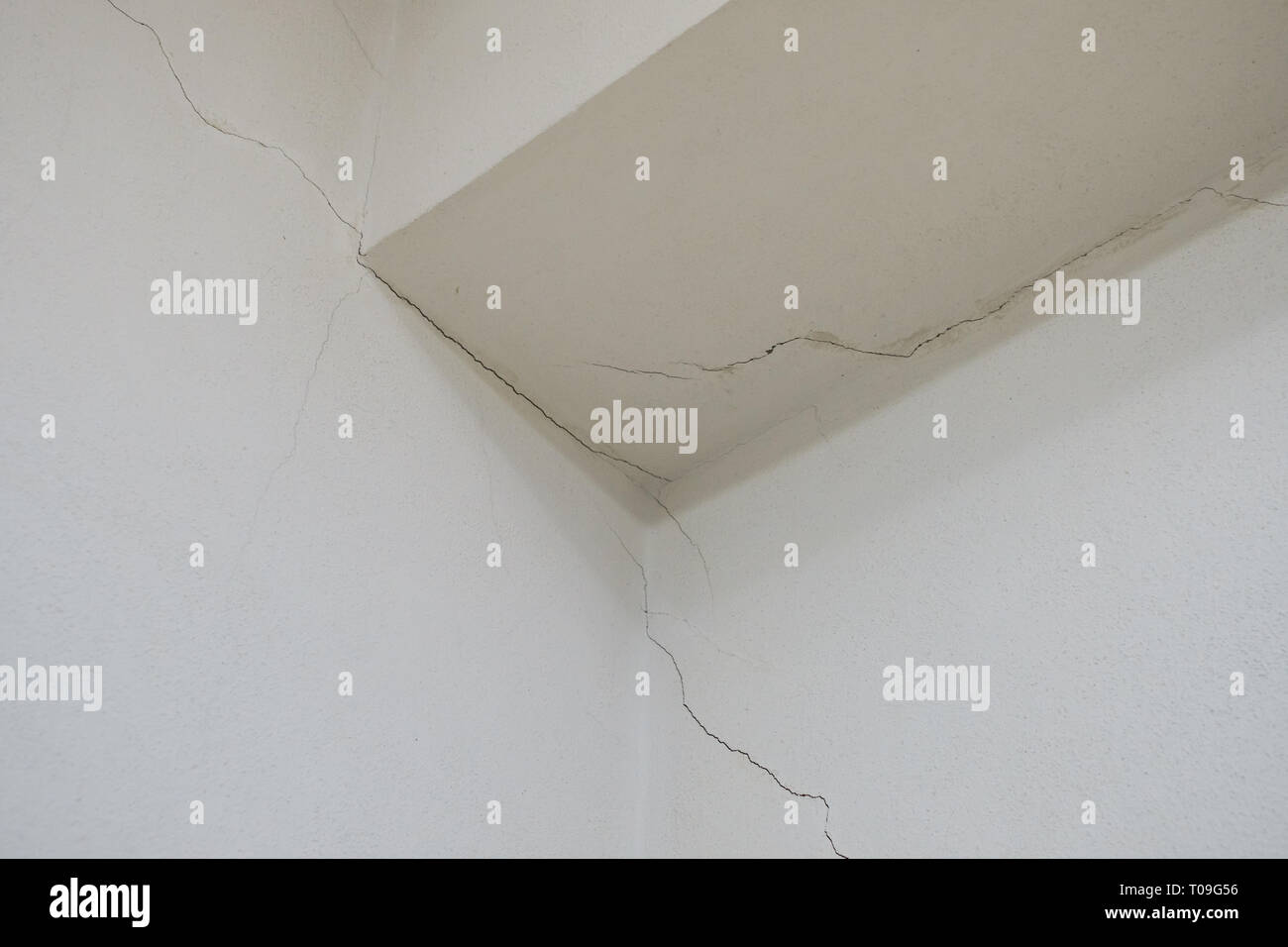 Uper corner of a white room with cracks on the wall, showing signs of a ...
