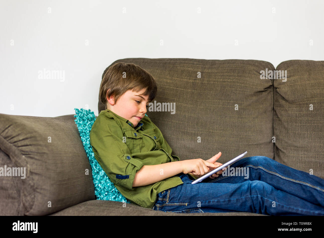 boy laying relaxed on sofa playing on his tablet Stock Photo - Alamy