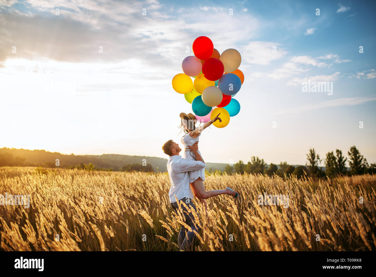 Happy husband hugs wife with balloons in wheat field. Pretty couple ...