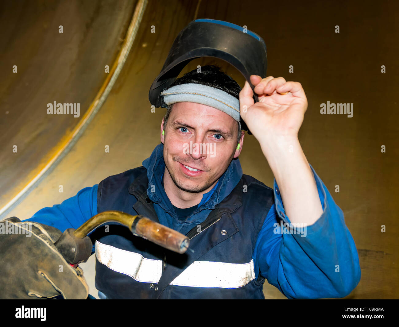 welder with mig/ mag welding gun in his hand, lifting his welding mask ...