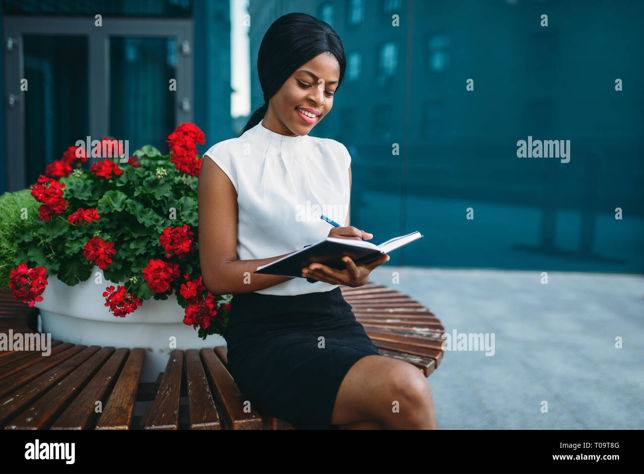 Businesswoman sitting on the bench and writes in notepad in front of ...