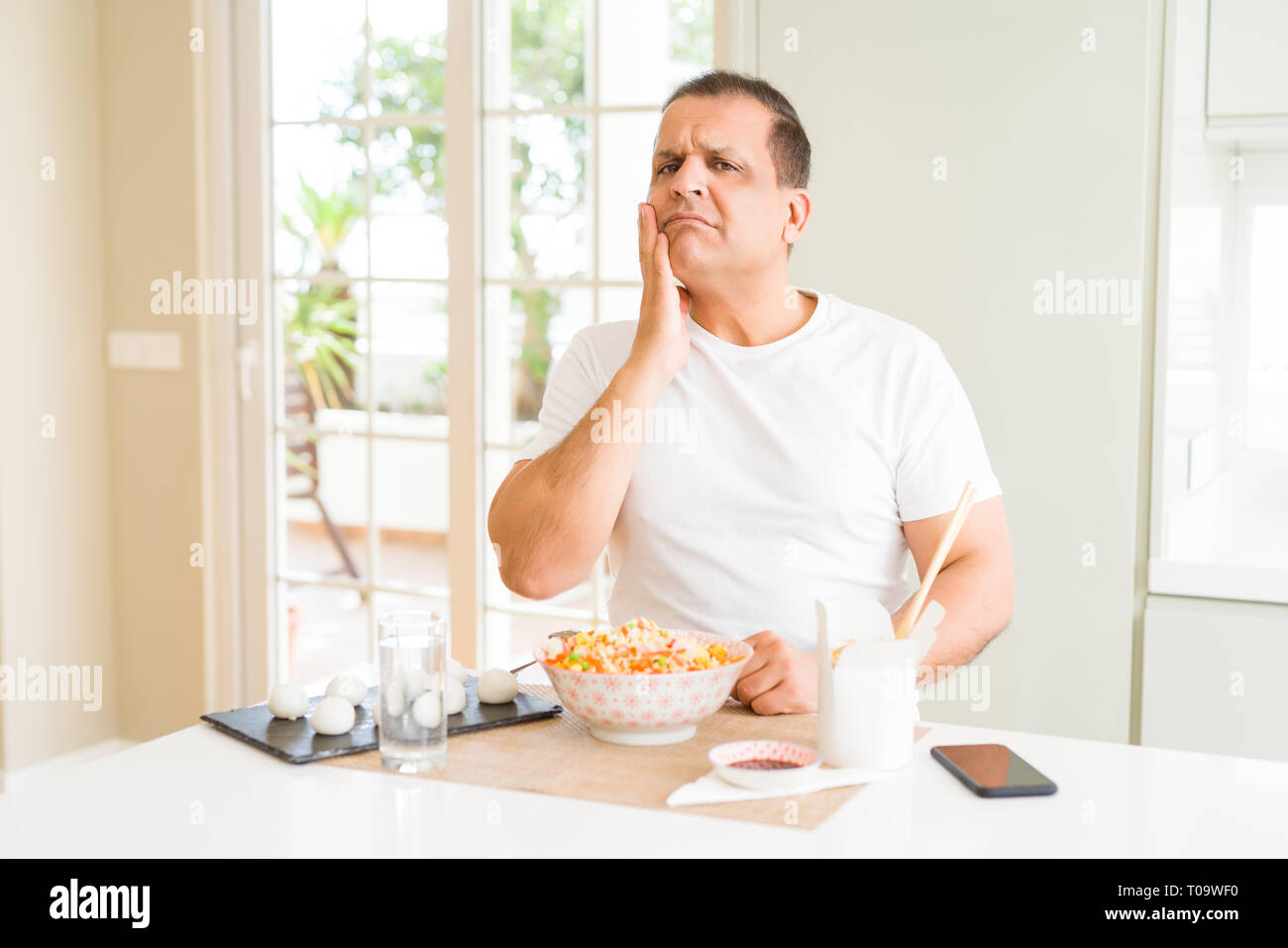 Middle age man eating asian food with chopsticks at home thinking ...