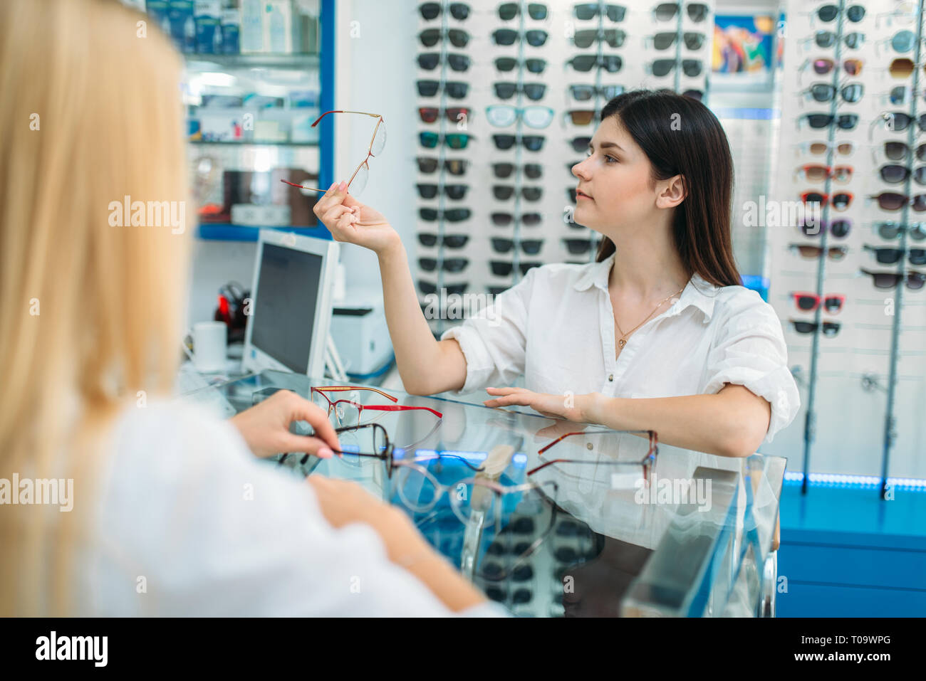 Female optician and consumer chooses glasses frame in optics store ...