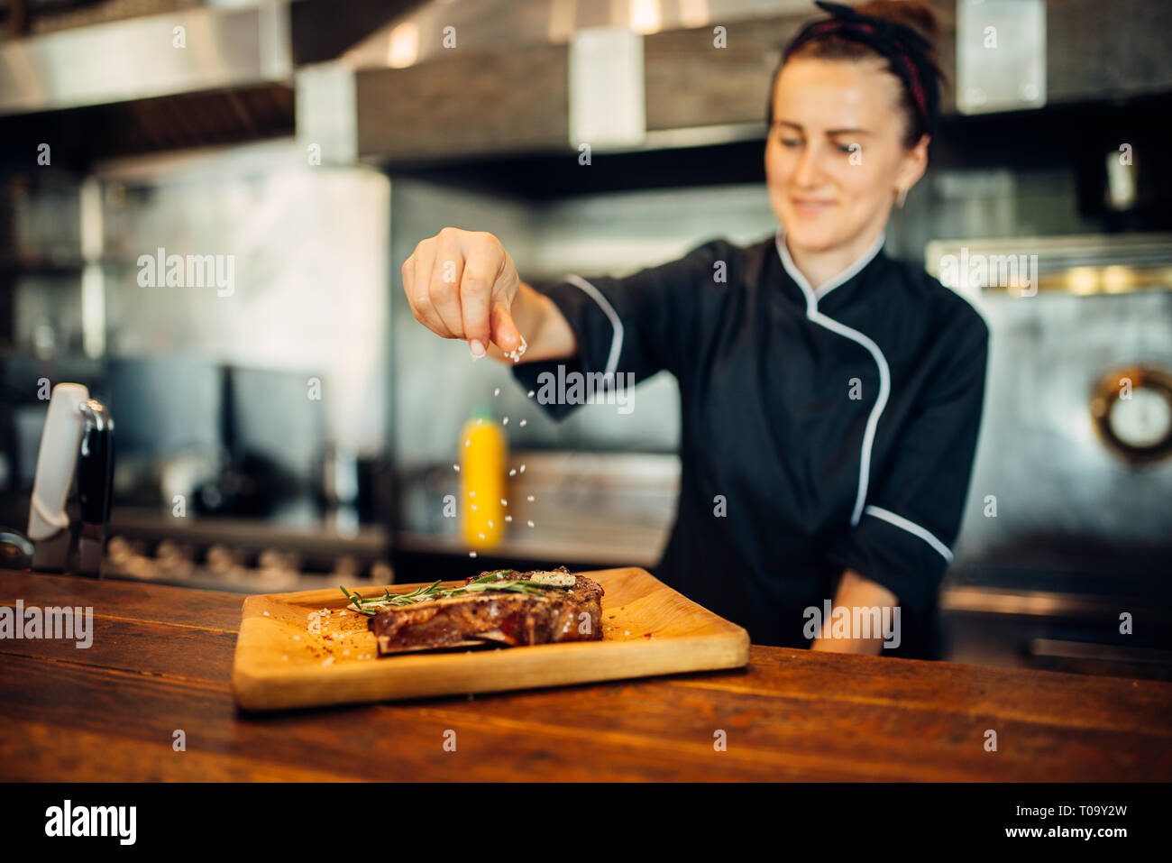 Female cook sprinkle with seasoning fresh prepared steak, grilled meat ...