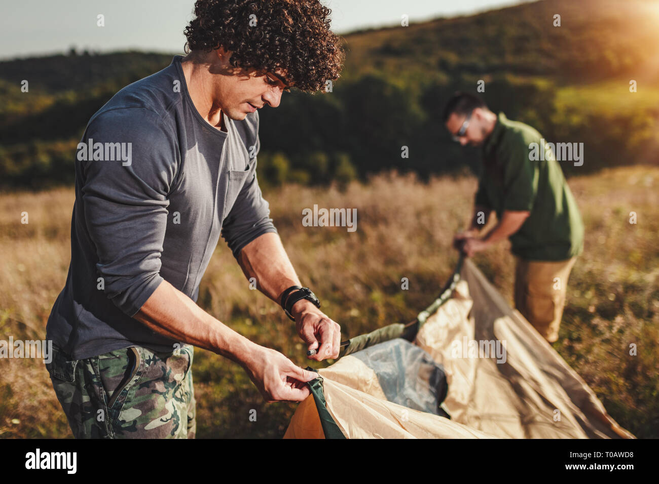 The young happy friends are preparing for camping. They're installing a ...