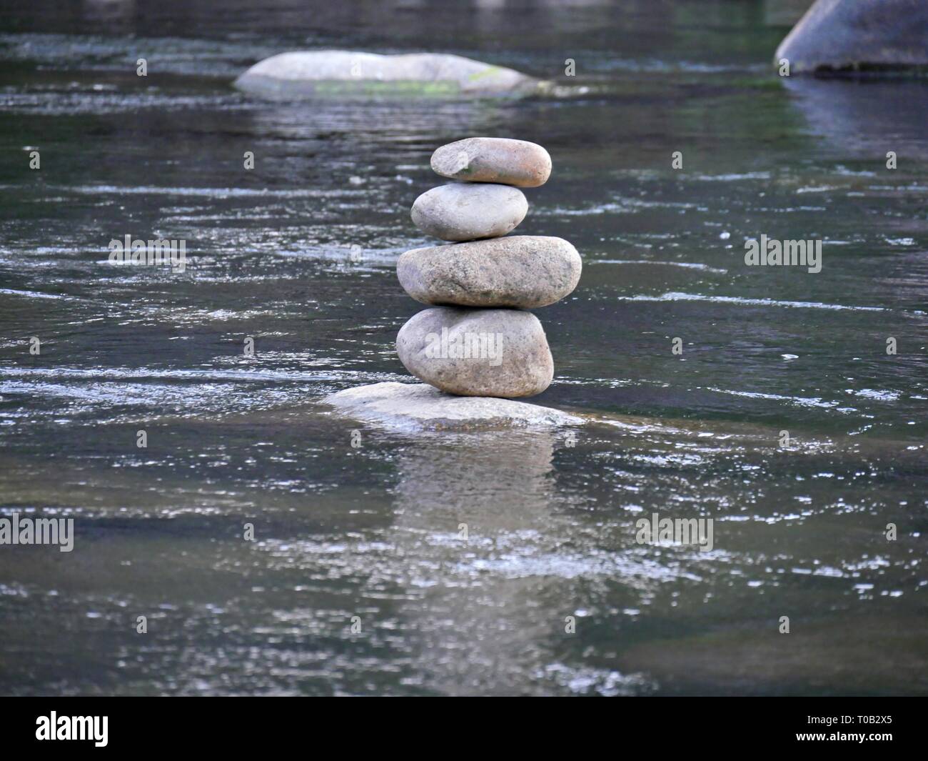 Wide shot of a of a stack of stones on top of a big rock in the river ...