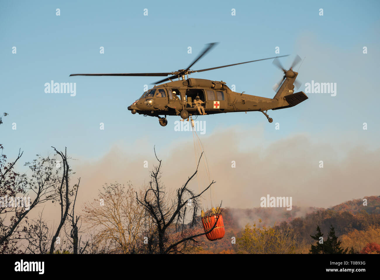A Red Cross helicopter carries water from a nearby stream to extinguish ...