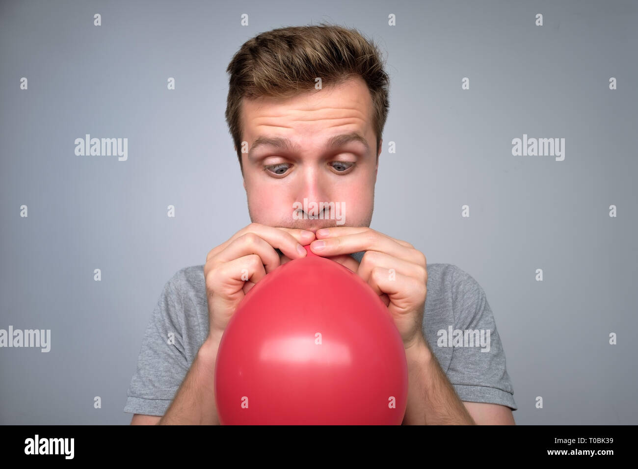 Young european man blowing up a red balloon Stock Photo - Alamy
