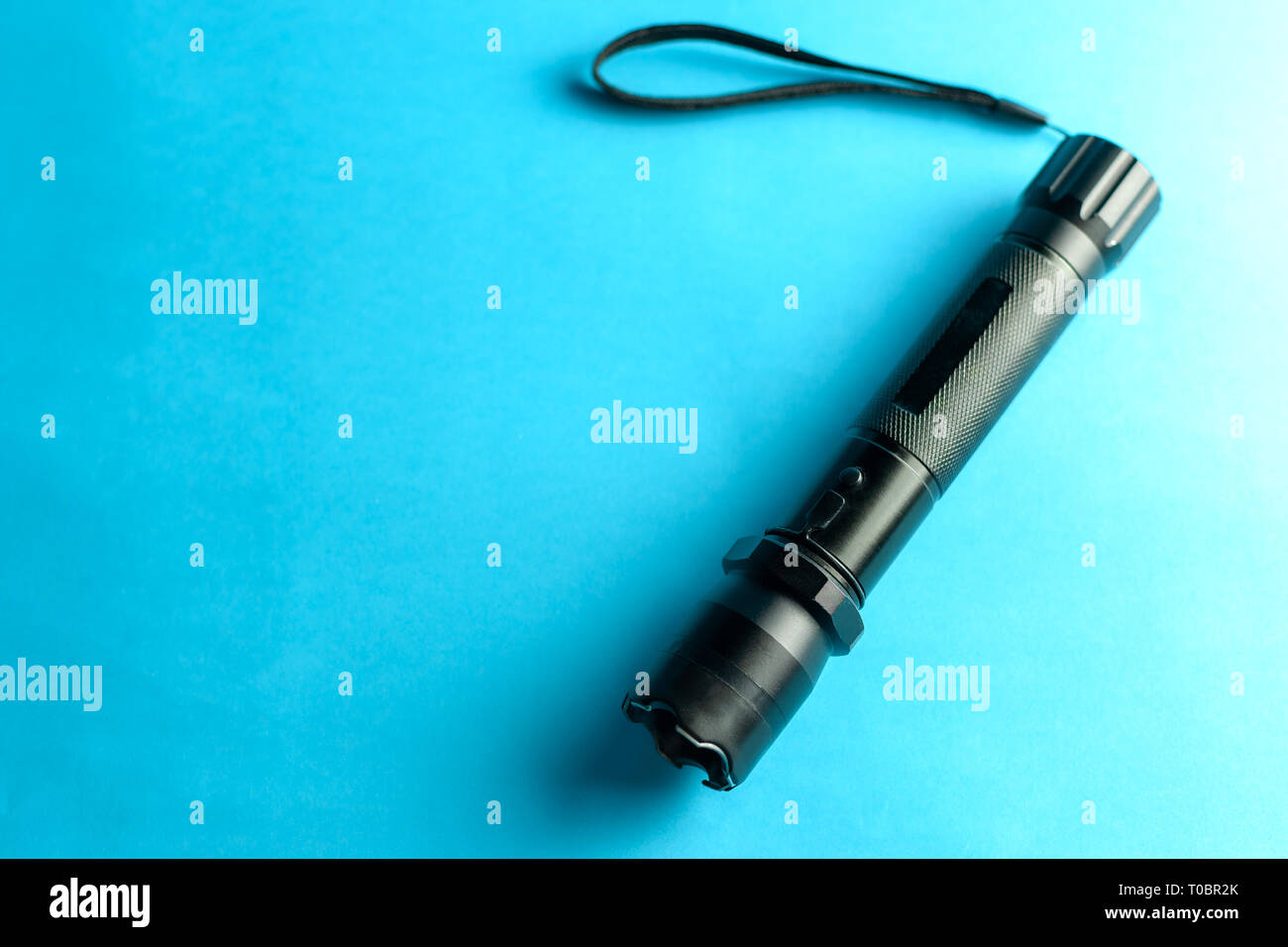 A black metal flashlight with shocker at the blue background ...