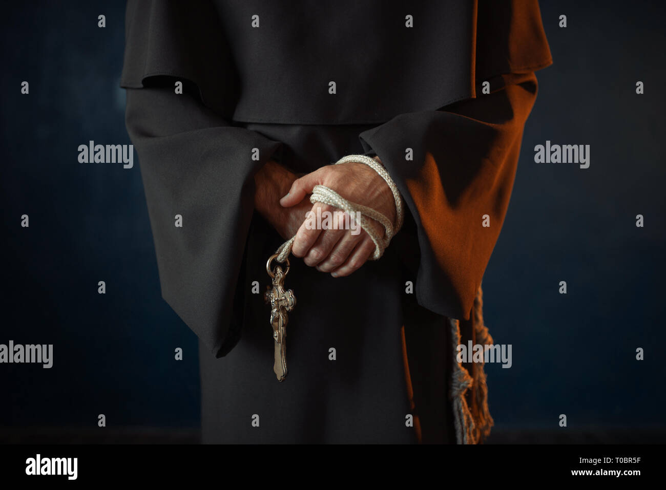 Male monk in black robe holds wooden rosary and cross in hands ...