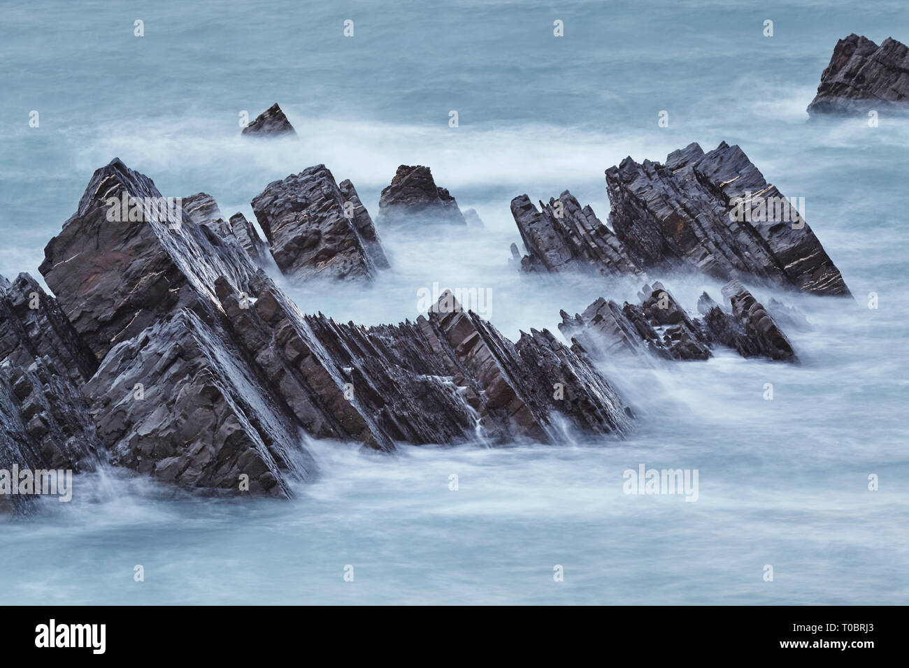 Atlantic surf washing around coastal rocks at dusk; at Hartland Quay ...