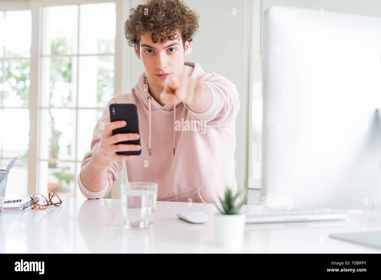 Young student man using smartphone and computer pointing with finger to ...
