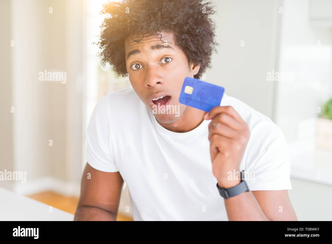 African American man holding credit card scared in shock with a ...