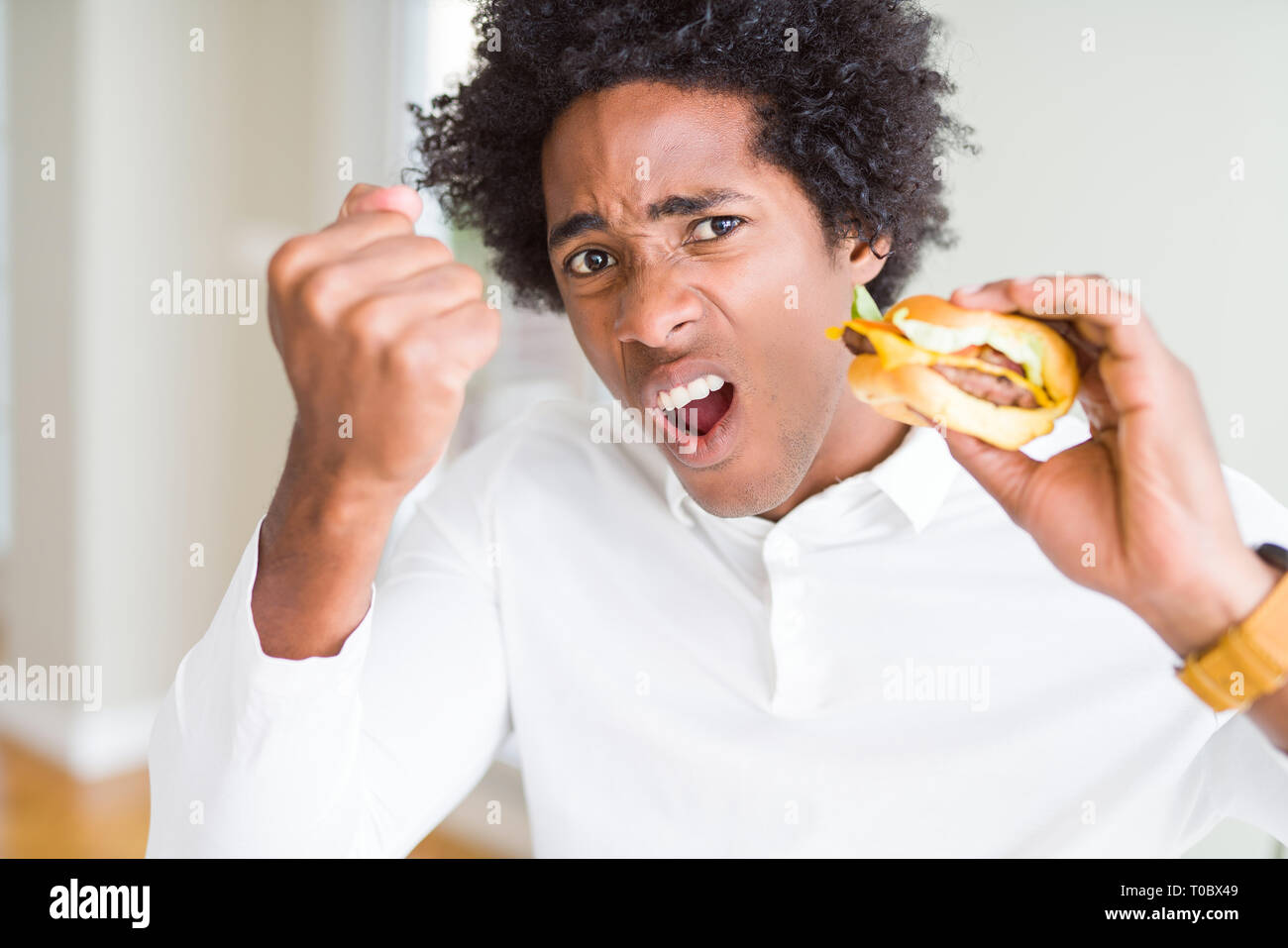 African American hungry man eating hamburger for lunch annoyed and ...