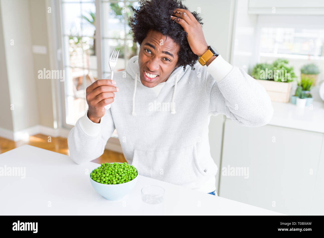 African American man eating fresh green peas at home stressed with hand ...