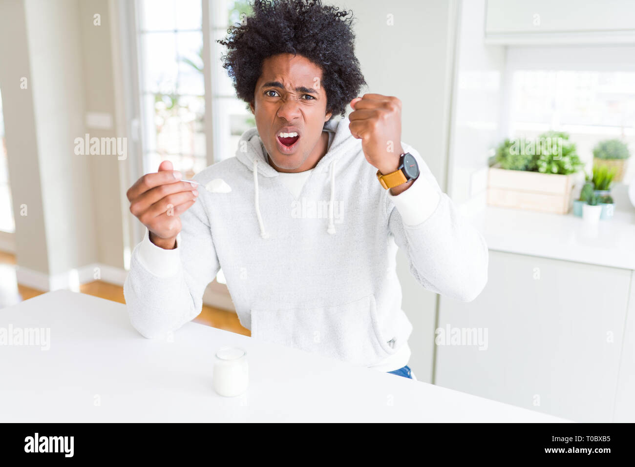 African American man eating healthy yogurt for breakfast annoyed and ...