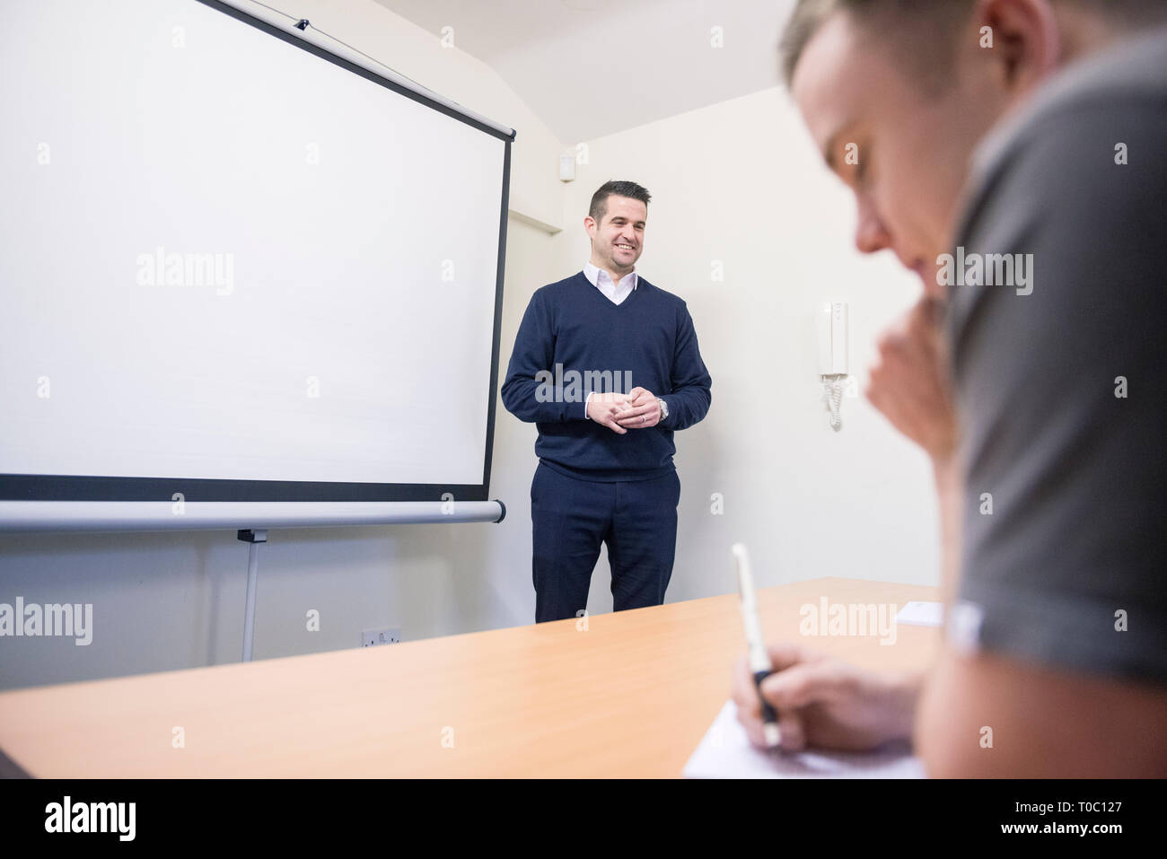 A white man in a blue jumper holds a training presentation for fellow ...