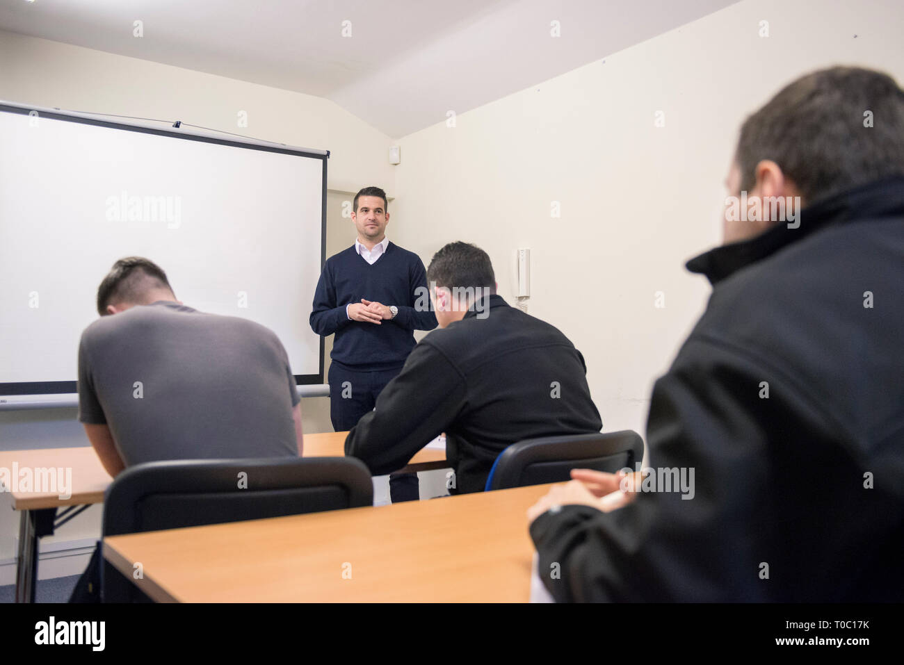 A white man in a blue jumper holds a training presentation for fellow ...
