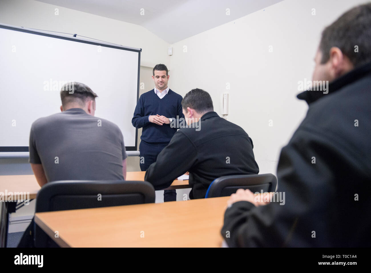 A white man in a blue jumper holds a training presentation for fellow ...