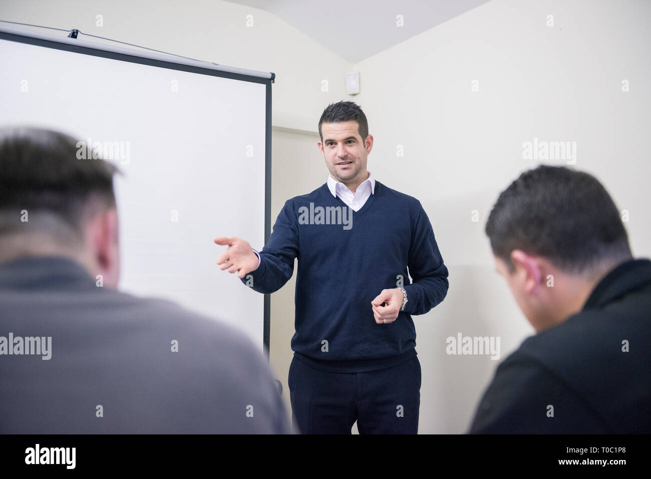 A white man in a blue jumper holds a training presentation for fellow ...