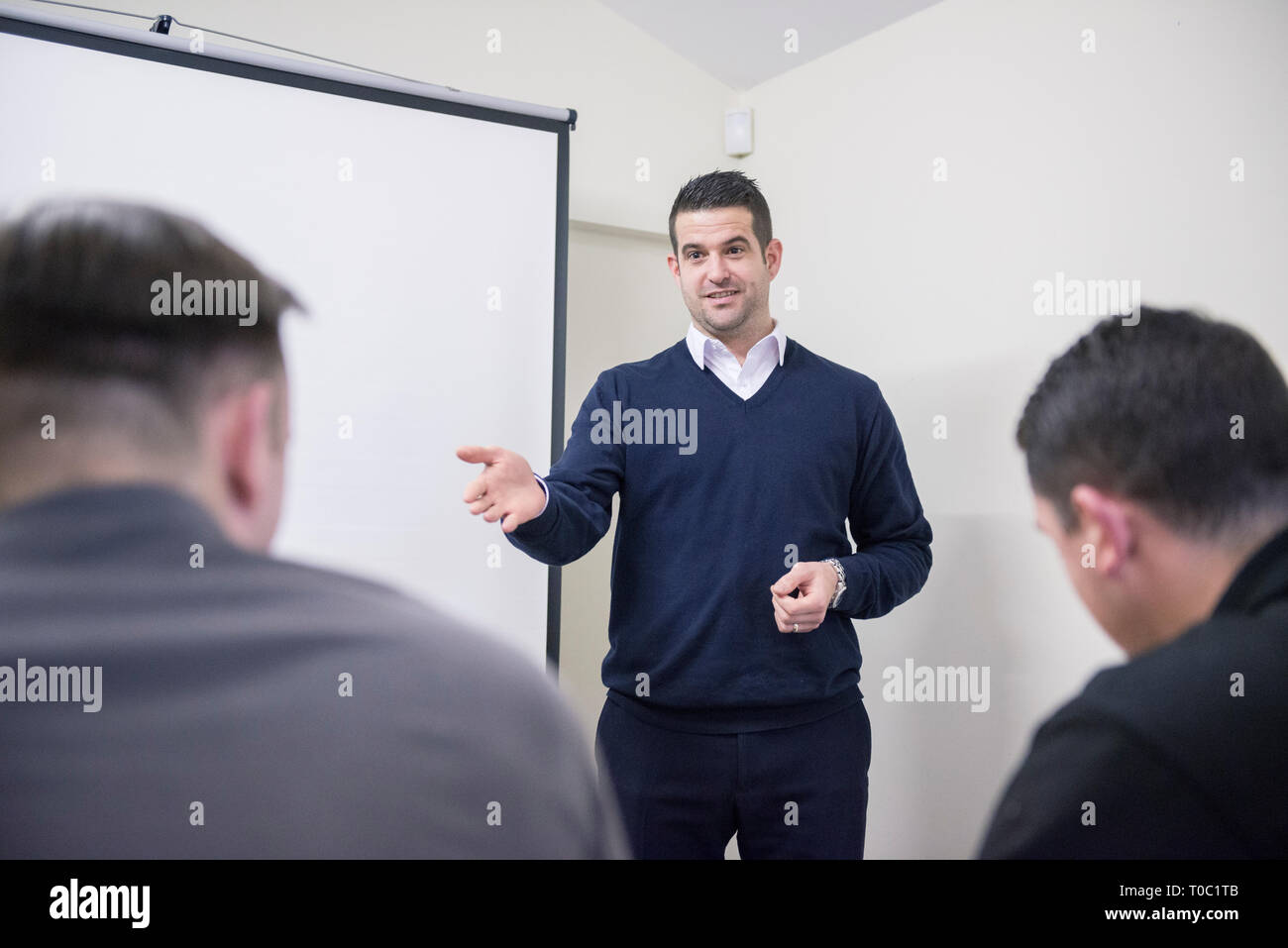 A white man in a blue jumper holds a training presentation for fellow ...