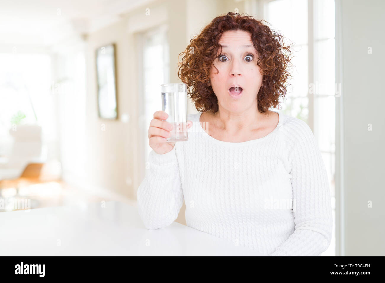 Senior woman driking a fresh glass of water scared in shock with a ...