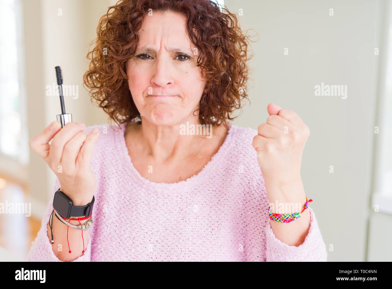 Senior woman putting mascara on eyelashes annoyed and frustrated ...