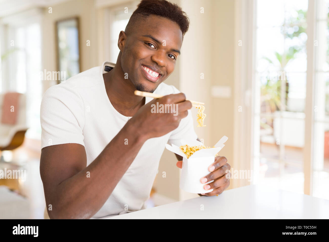 Handsome african man eating asian noodles in a delivery box, smiling ...