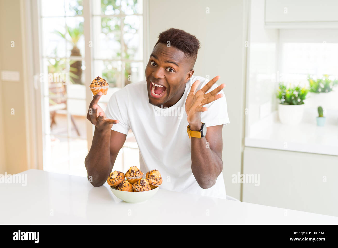 African american man eating chocolate chips muffin very happy and ...
