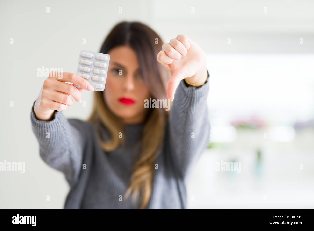 Young beautiful woman holding pharmaceutical pills at home with angry ...