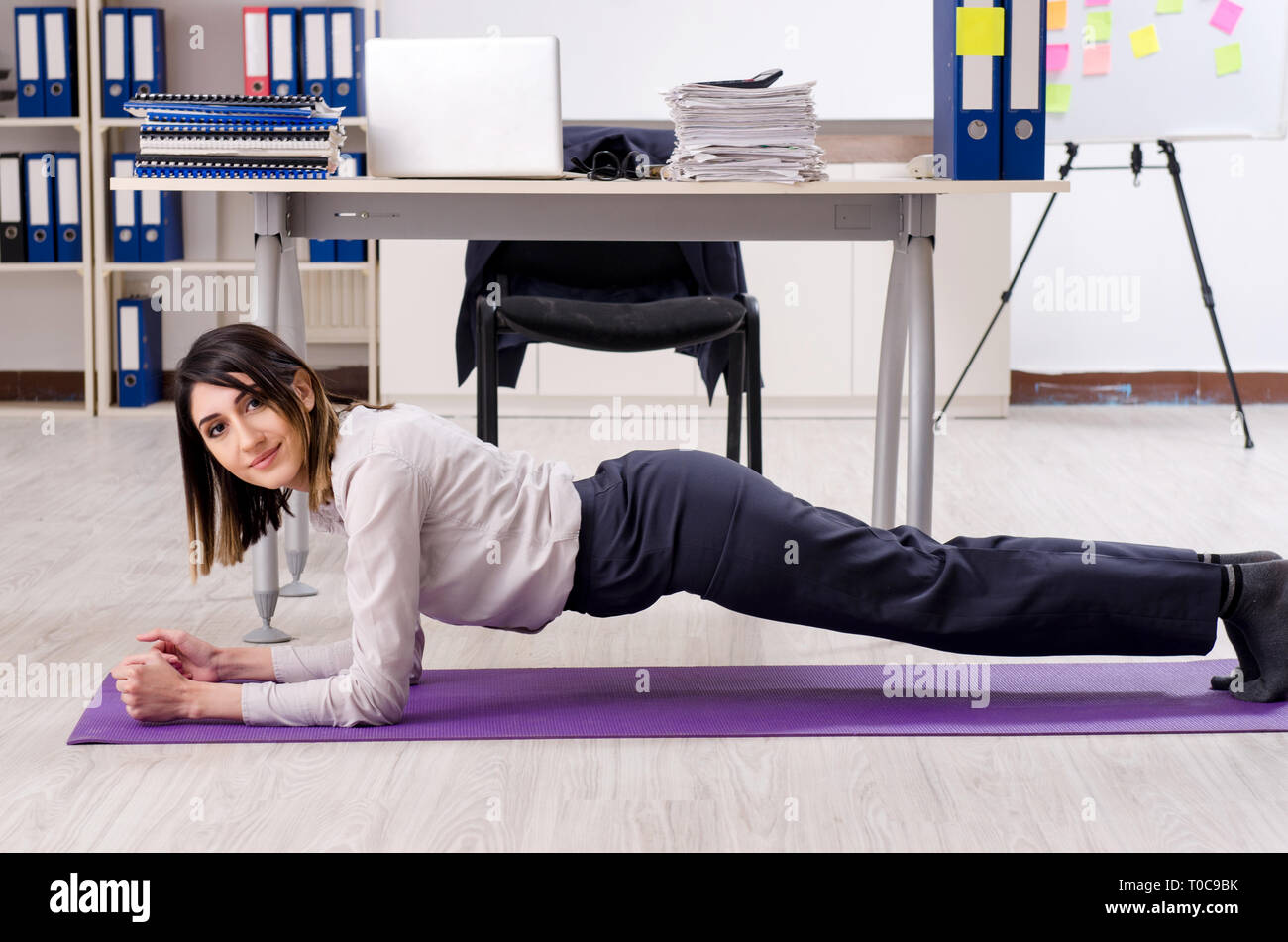 Young female employee doing exercises at workplace Stock Photo - Alamy