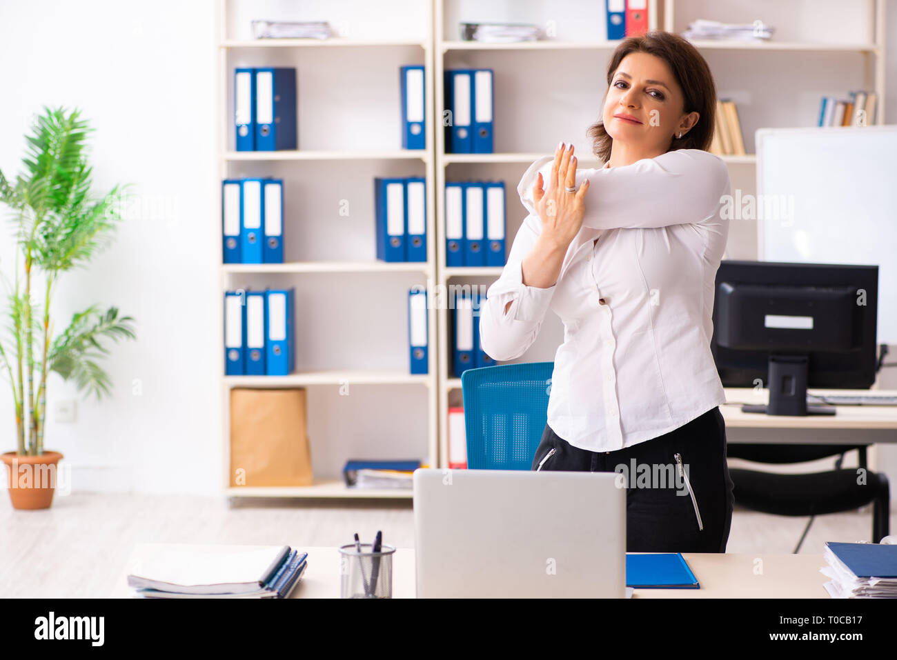 Middle-aged female employee doing exercises in the office Stock Photo ...