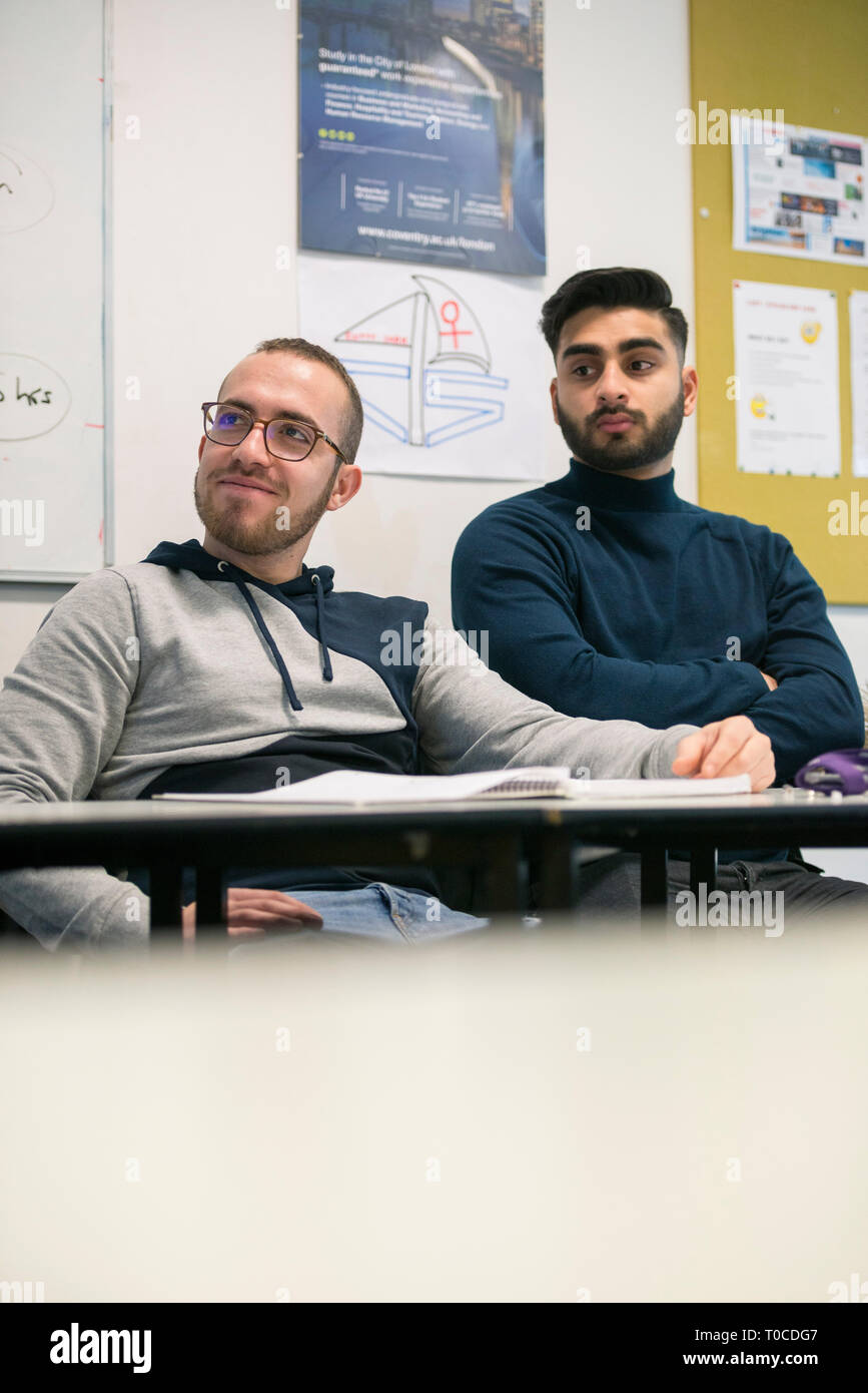 pupils and students in a classroom at a college / university, being taught a lesson while in ...