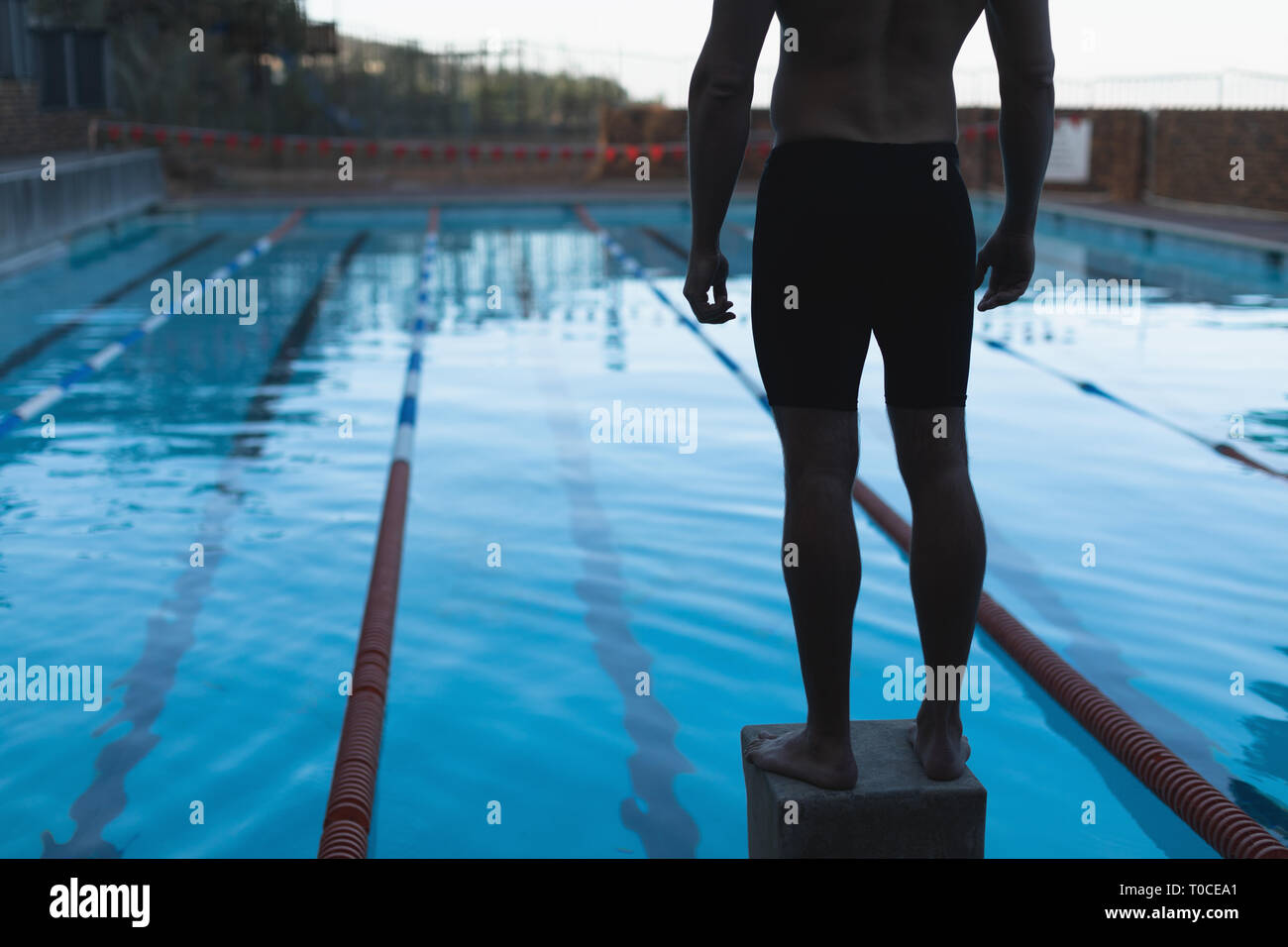 Male swimmer standing standing on the starting block in front of the ...