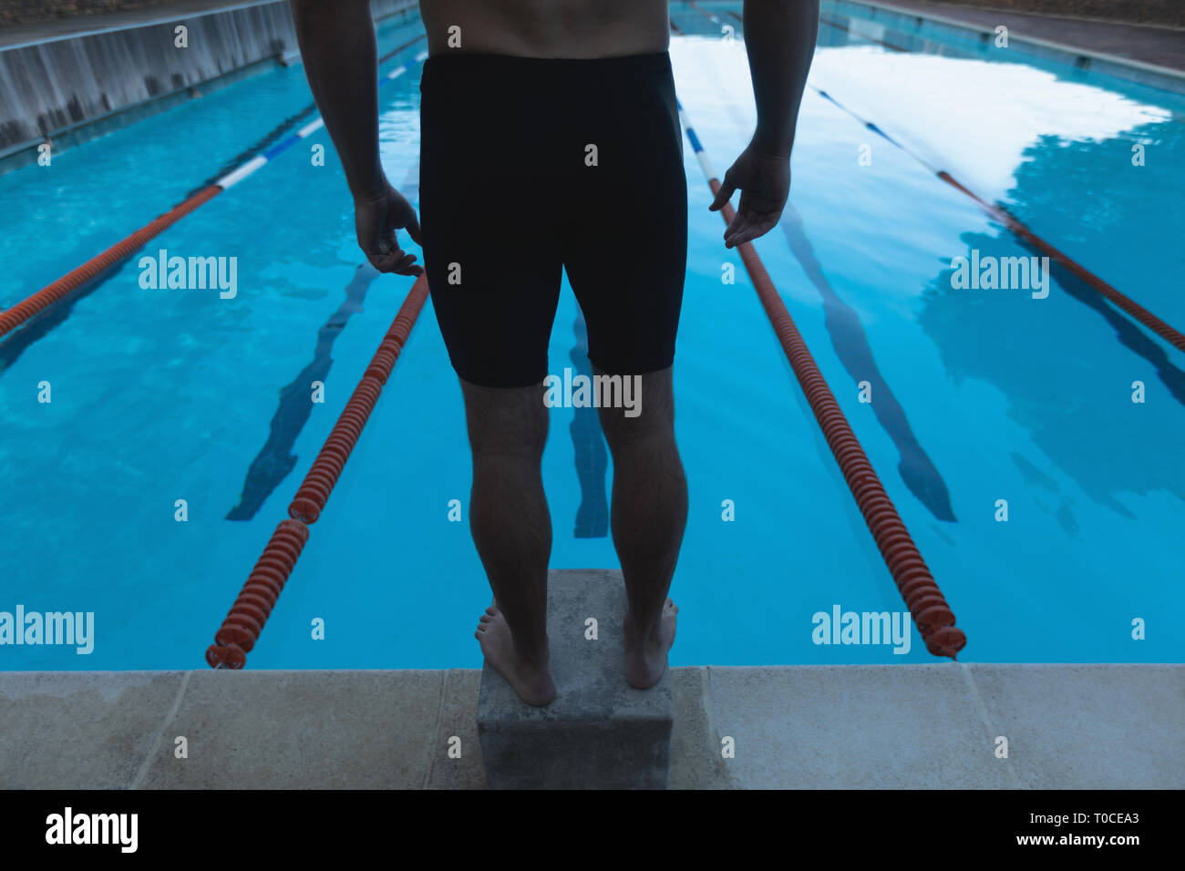 Male swimmer standing standing on the starting block in front of the ...