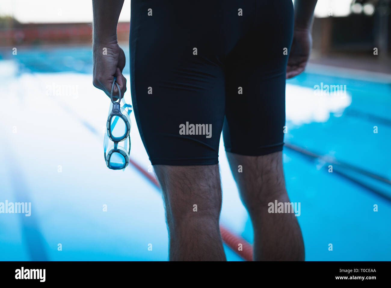 Male Swimmer Standing In Front Of The Swimming Pool With Swim Goggle
