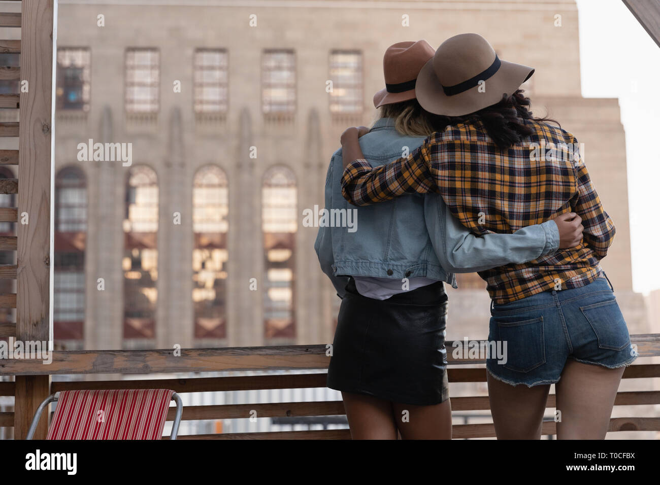 Female friends standing with arm around in balcony at home Stock Photo ...