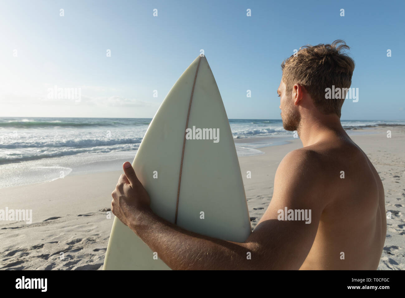 Young Caucasian male surfer with a surfboard standing on a beach Stock ...