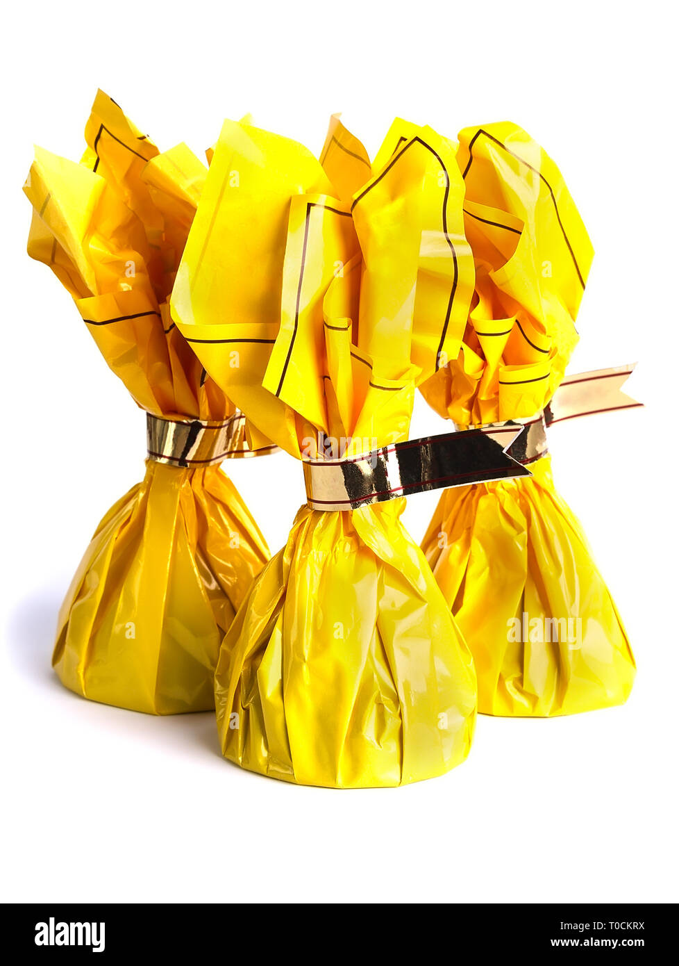 Three chocolates in a yellow wrapping with silver ribbons on a white ...