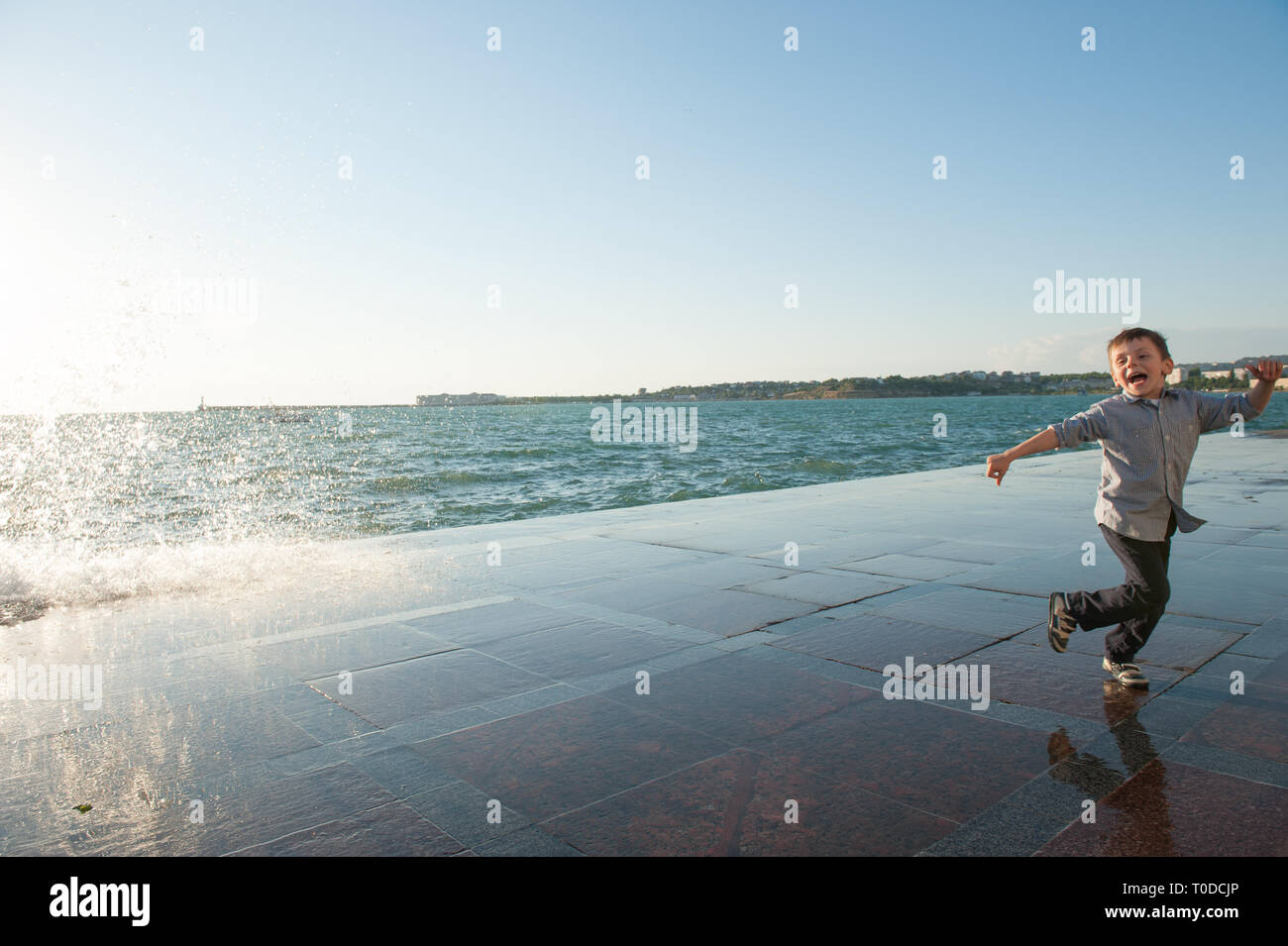 funny little boy running away from splash of waves on sea shore in city ...
