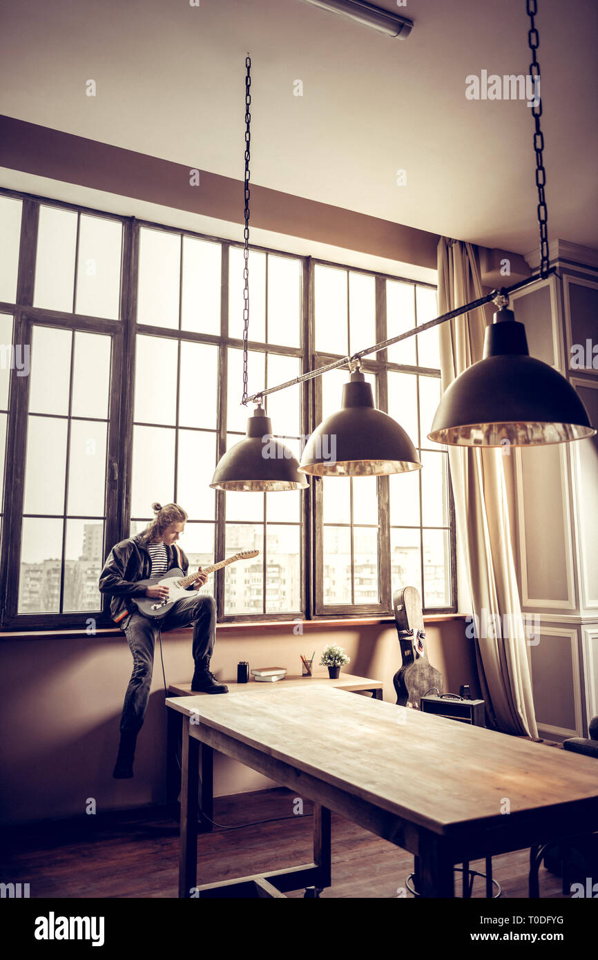 Rock musician sitting on the window sill in spacious room Stock Photo ...