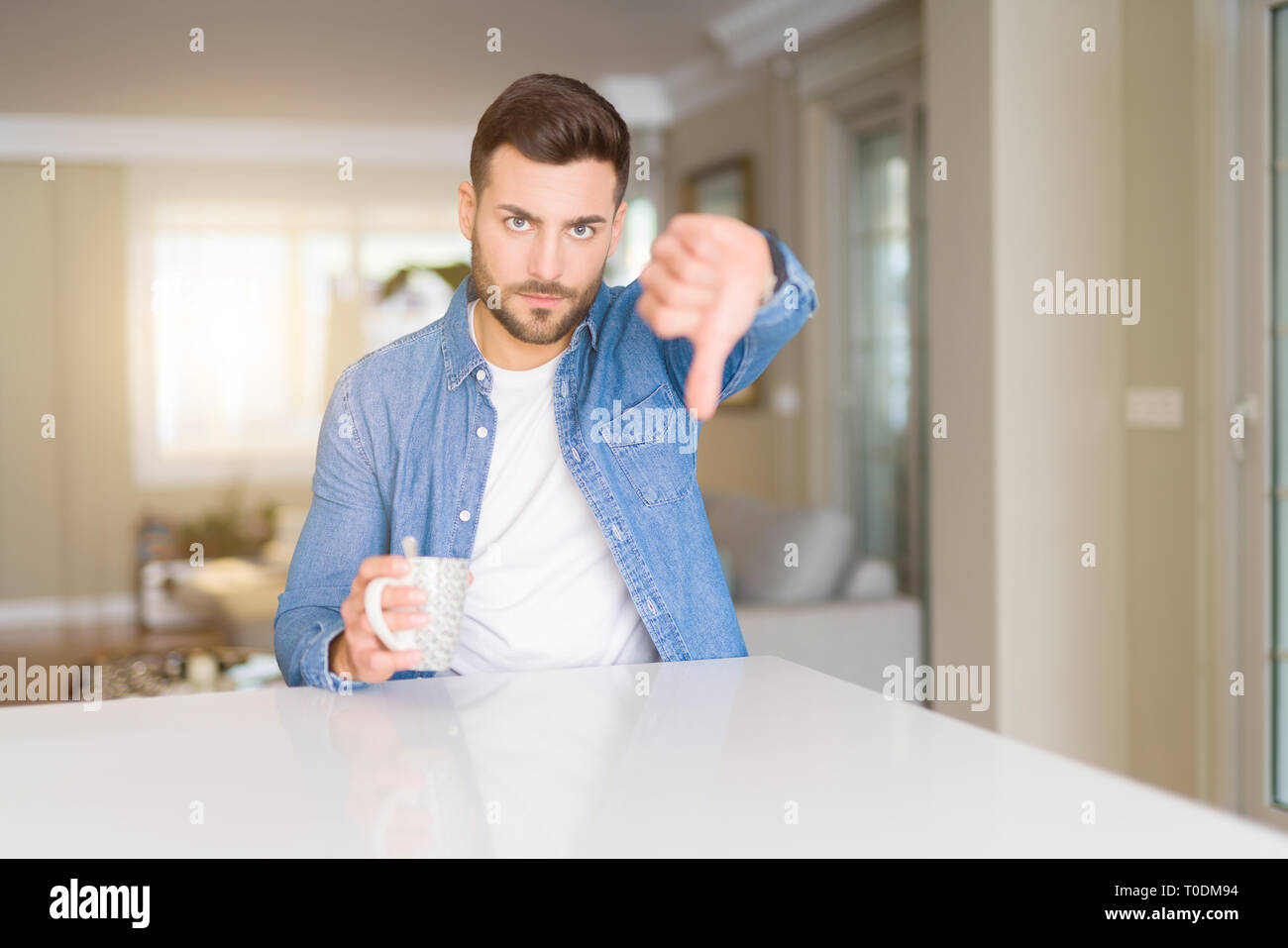 Young handsome man drinking a cup of coffee at home with angry face ...