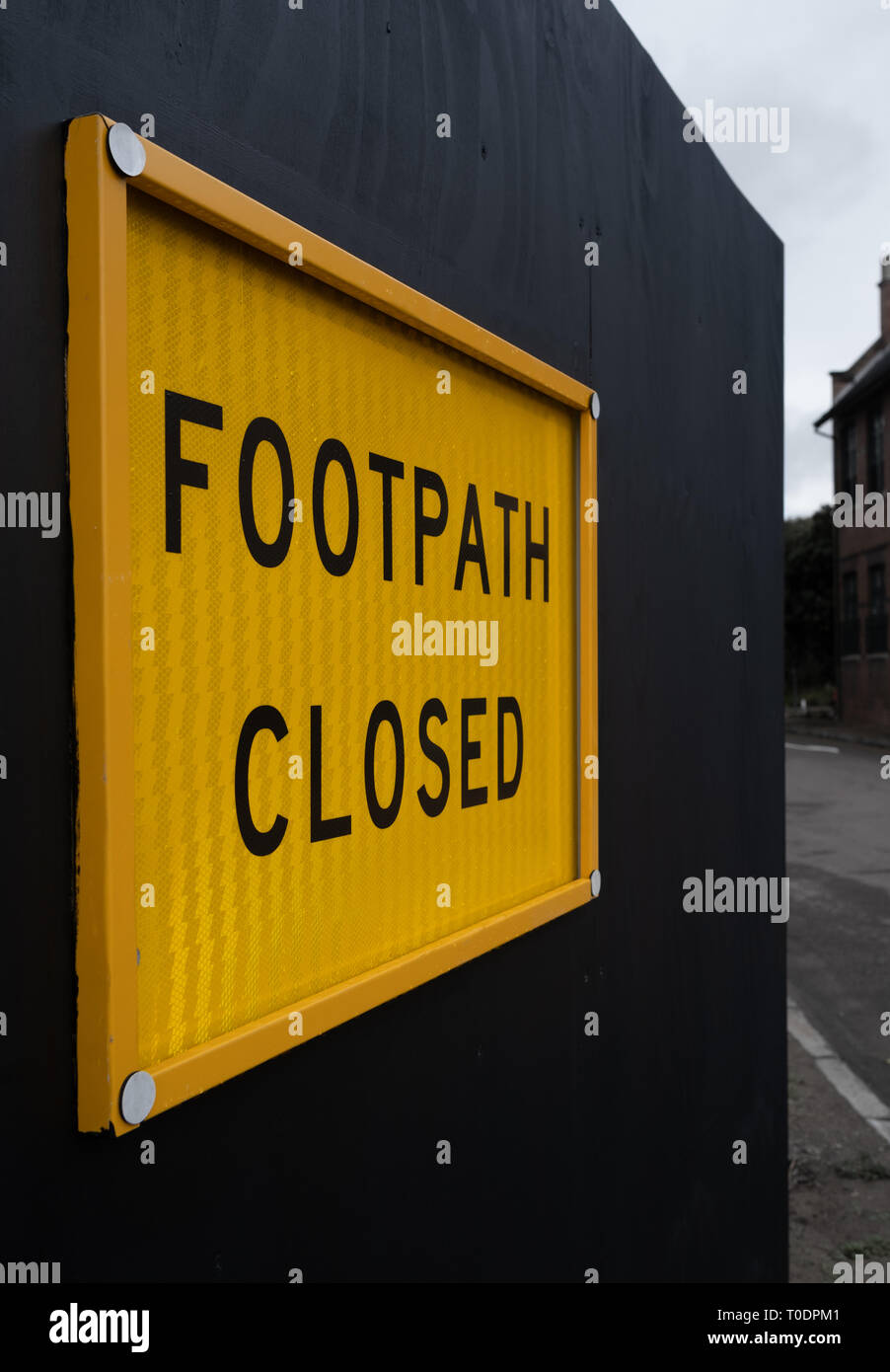 Yellow, footpath closed safety sign on a black fence outside a ...