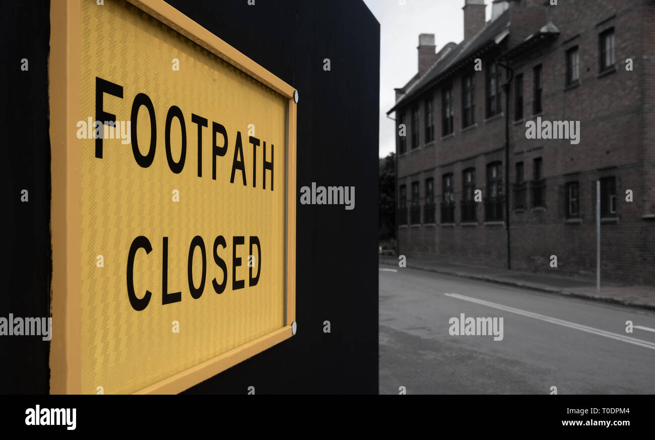 Yellow, footpath closed safety sign on a black fence outside a ...