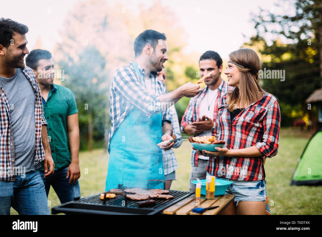 Happy friends grilling meat and enjoying barbecue party Stock Photo - Alamy