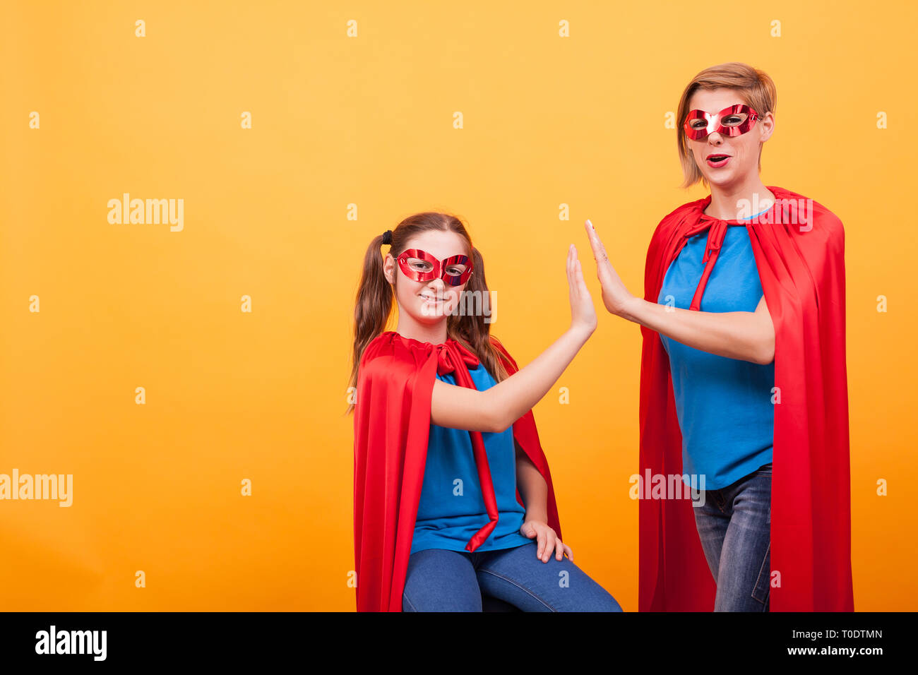 Mother and daughter dressed like superheros giving hi5 over yellow ...