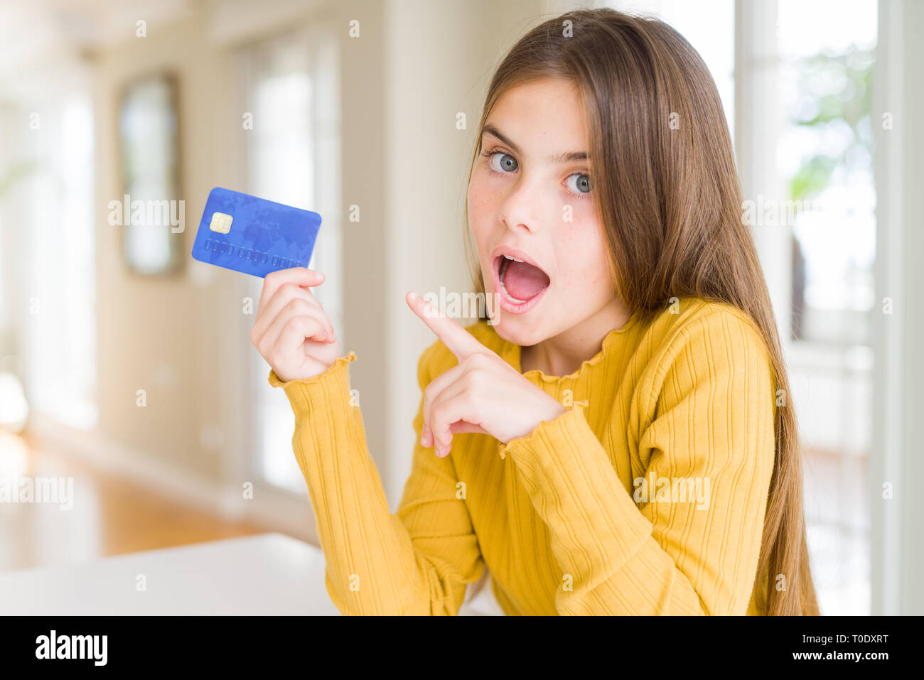 Beautiful young girl kid holding credit card very happy pointing with ...